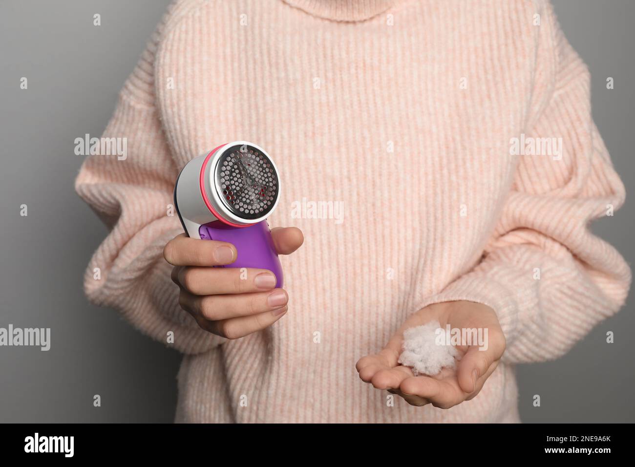 Woman in woolen sweater holding fabric shaver and lint on light grey ...