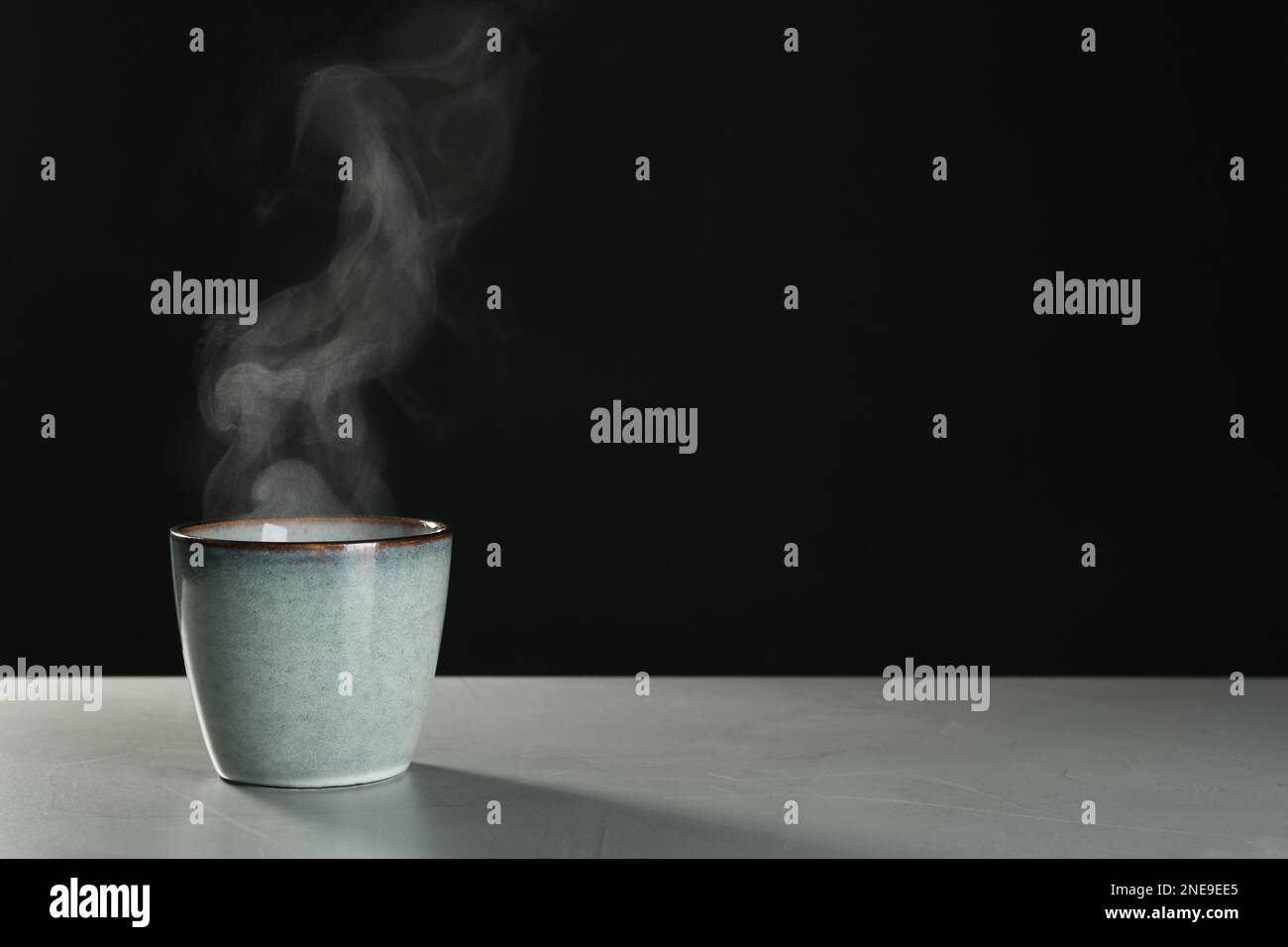 Mug with steam on table against black background. Space for text Stock ...