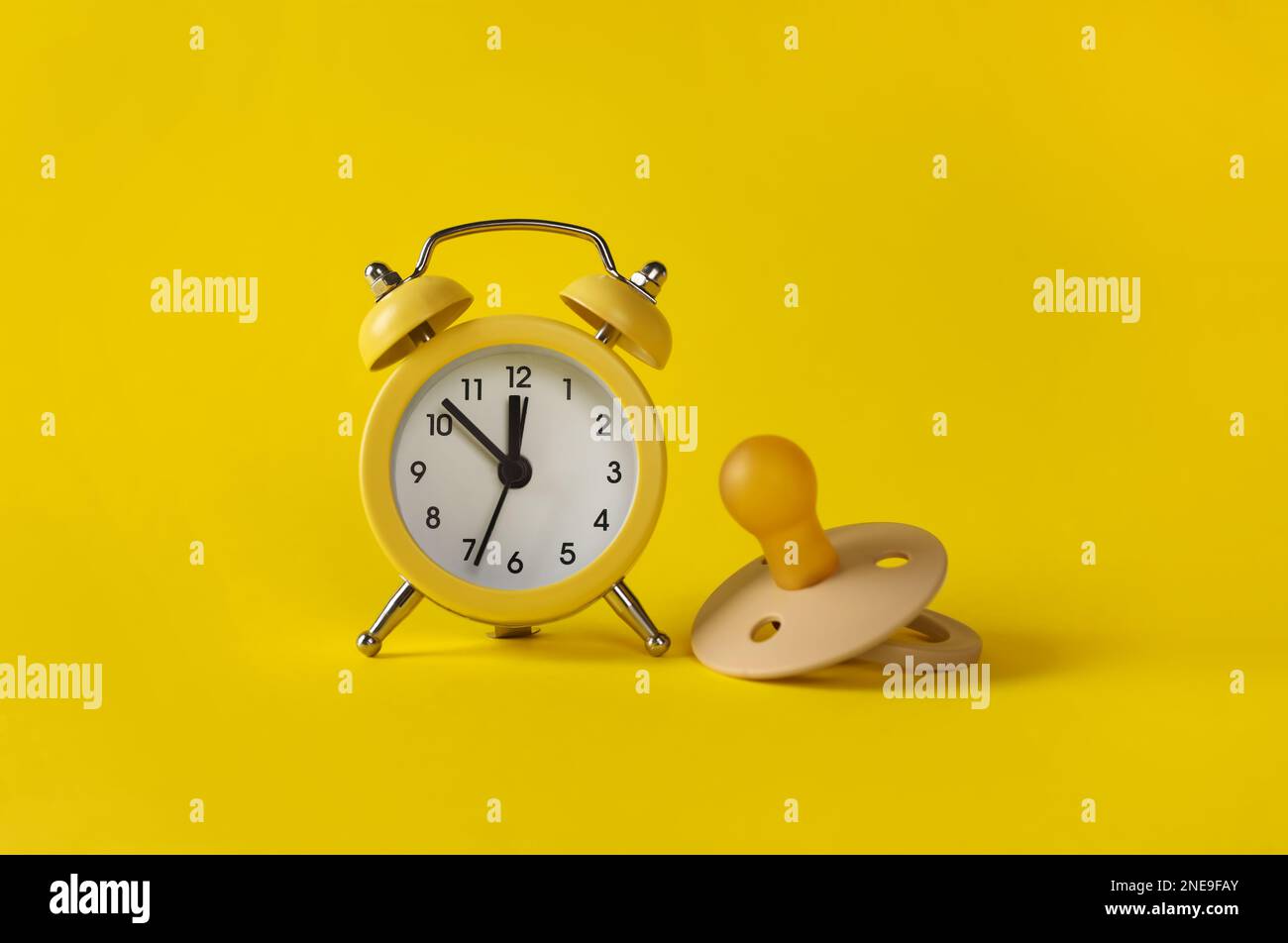 Alarm clock and baby dummy on yellow background. Time to give birth ...