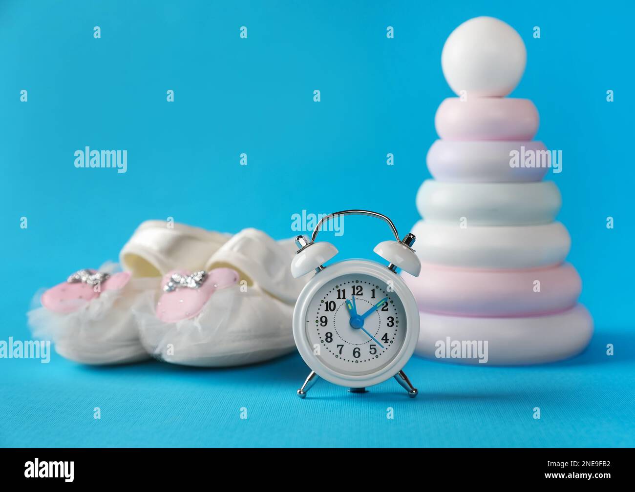 Alarm clock, toy pyramid and baby booties on light blue background ...