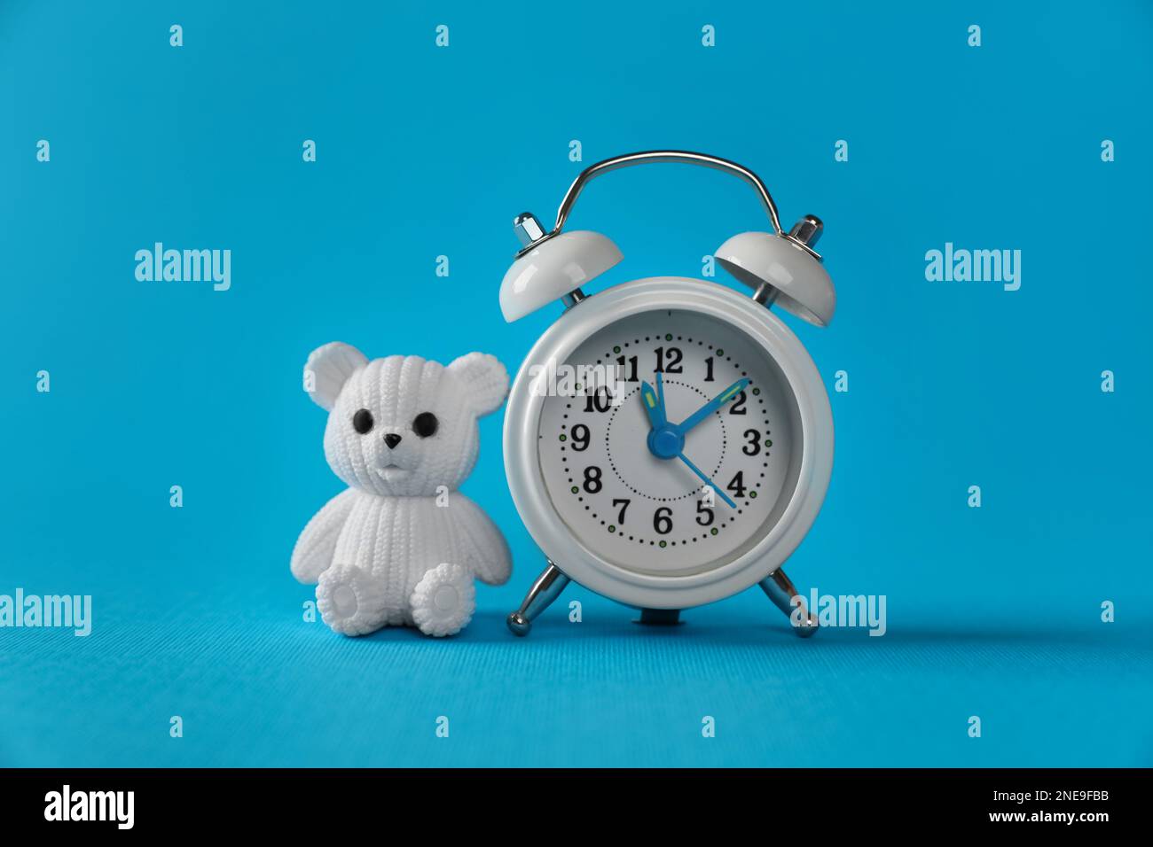 Alarm clock and toy bear on light blue background. Time to give birth ...
