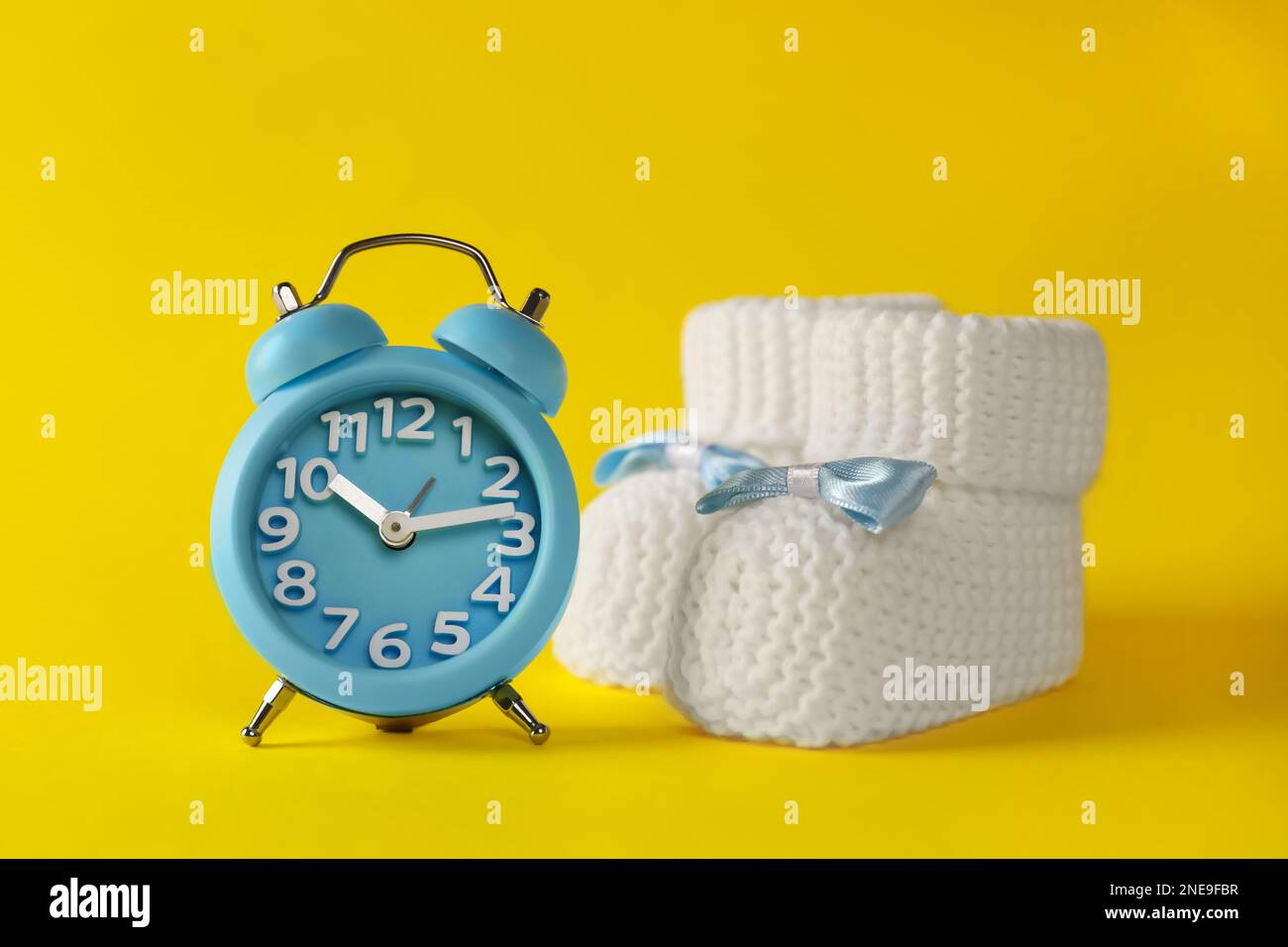 Alarm clock and baby booties on yellow background. Time to give birth ...