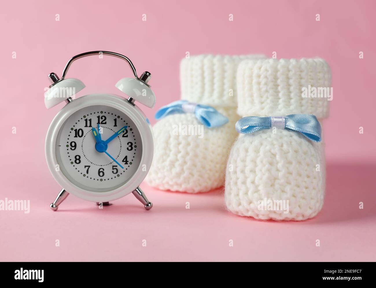 Alarm clock and baby booties on pink background. Time to give birth ...