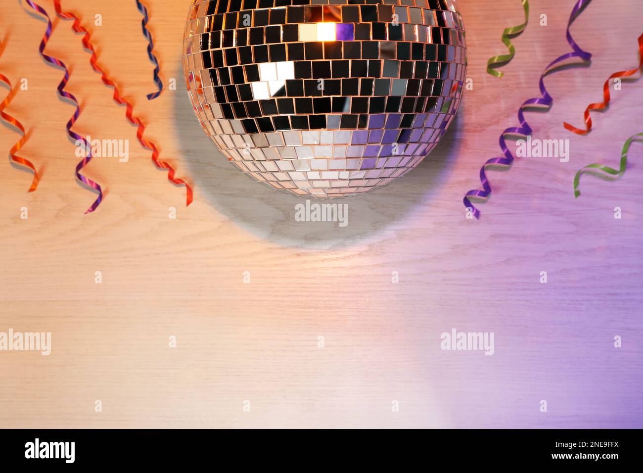 Shiny disco ball and serpentine streamers on white wooden background ...