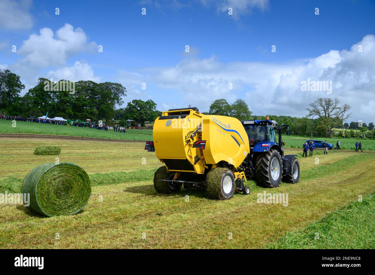 New Holland tractor with baler making big round bales in a meadow on a ...