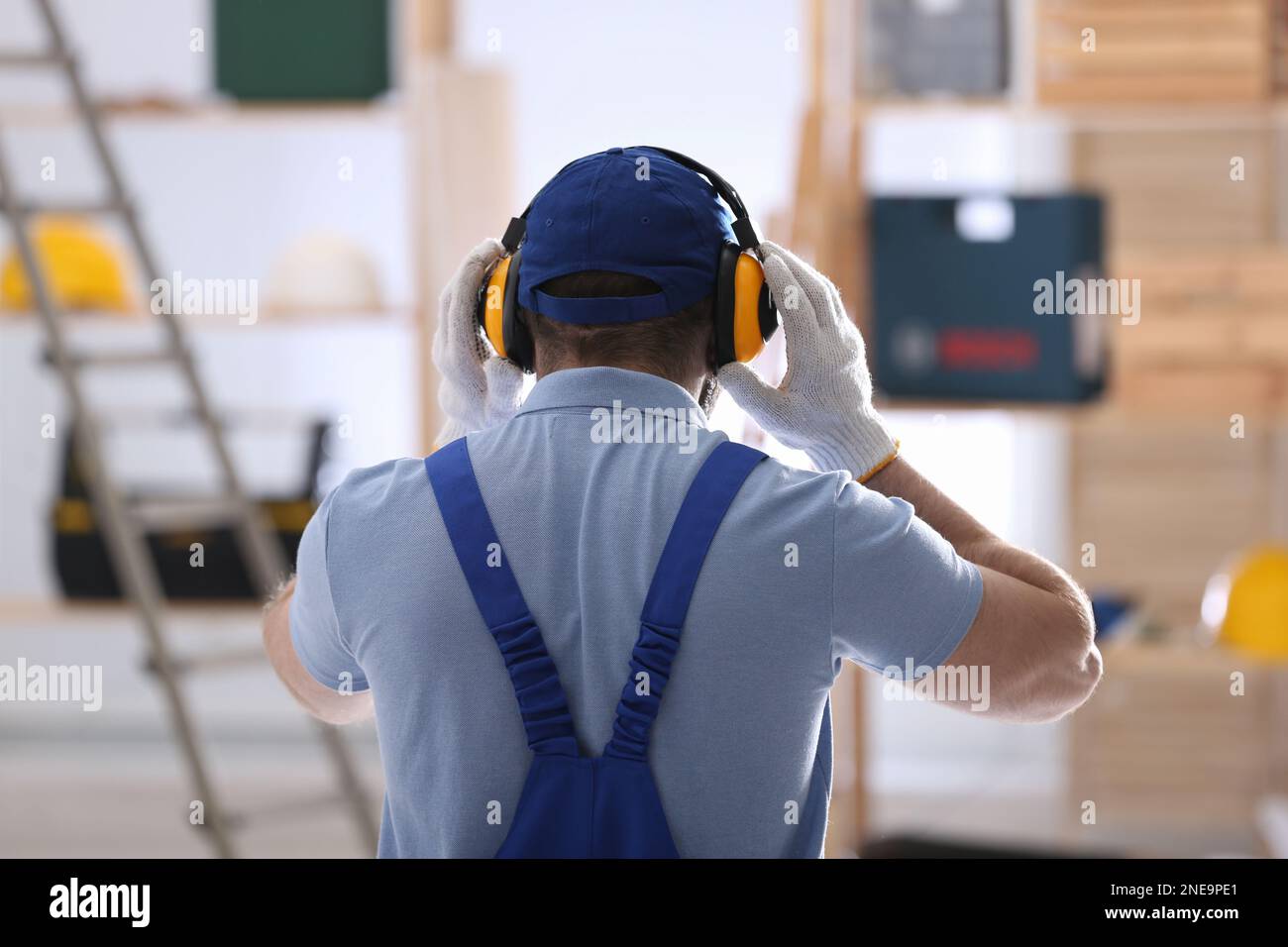 Worker wearing safety headphones indoors, back view. Hearing protection ...