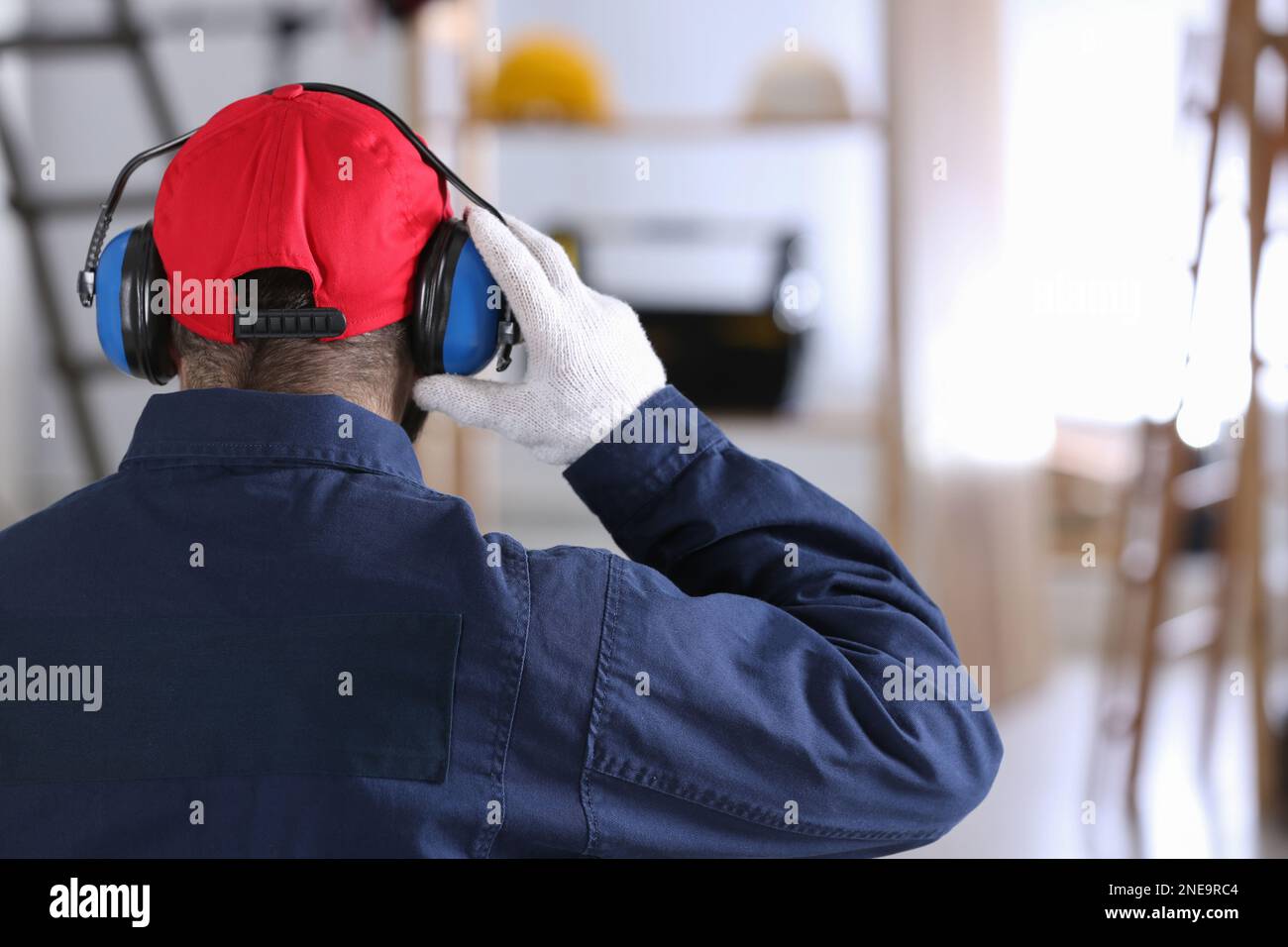 Worker wearing safety headphones indoors, back view. Hearing protection ...