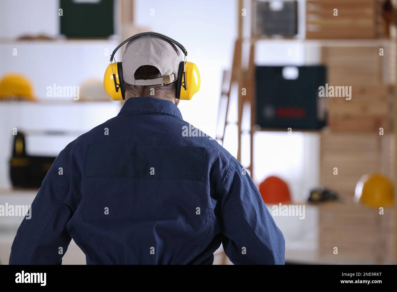Worker wearing safety headphones indoors, back view. Hearing protection ...
