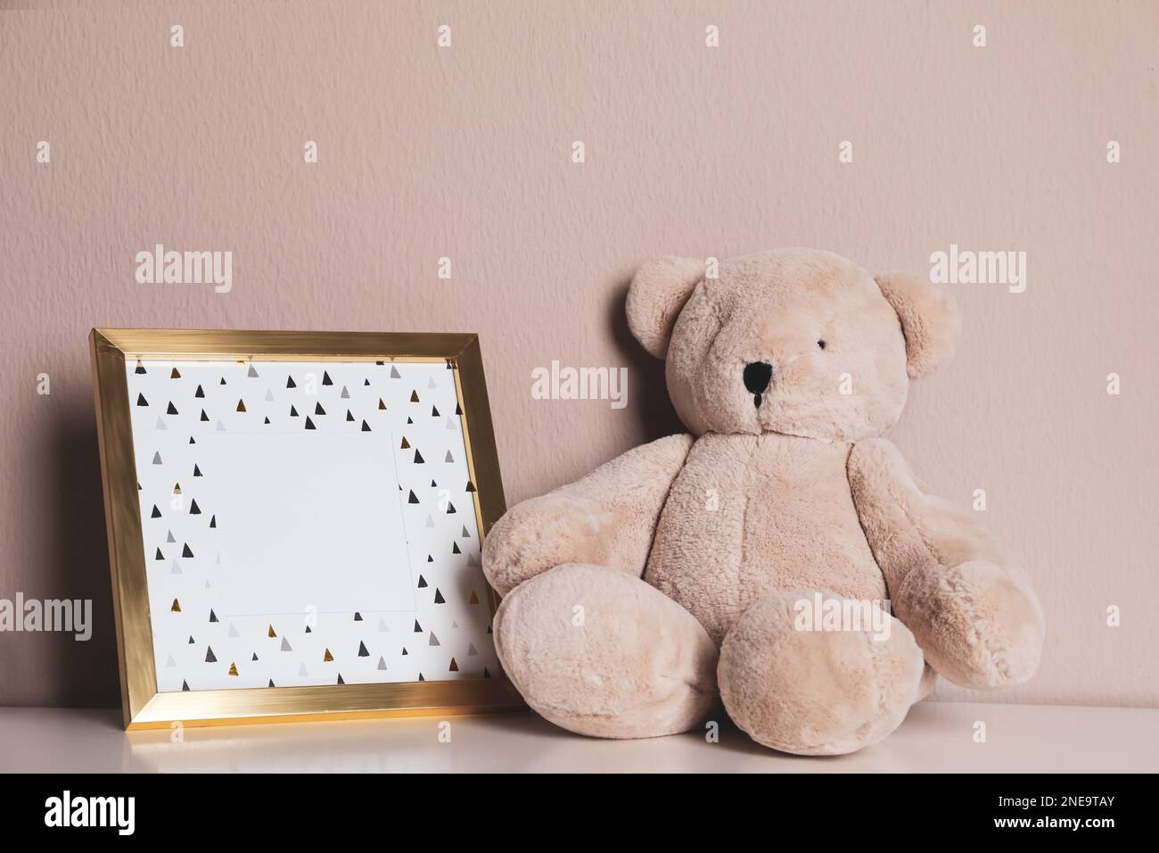 Empty photo frame and teddy bear on white table near grey wall. Space ...