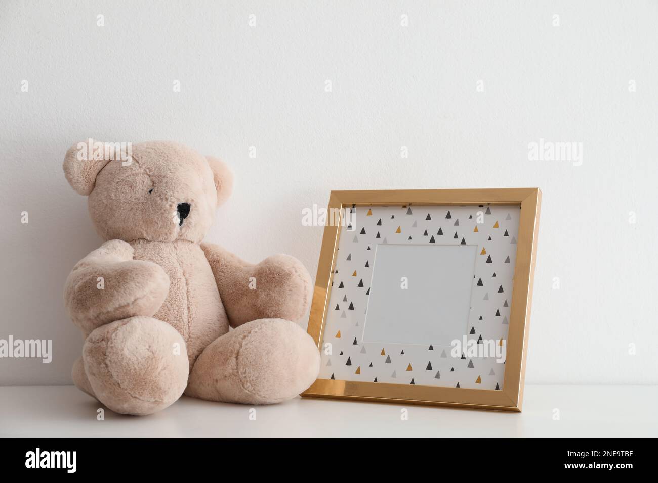 Empty photo frame and teddy bear on table near white wall. Space for ...