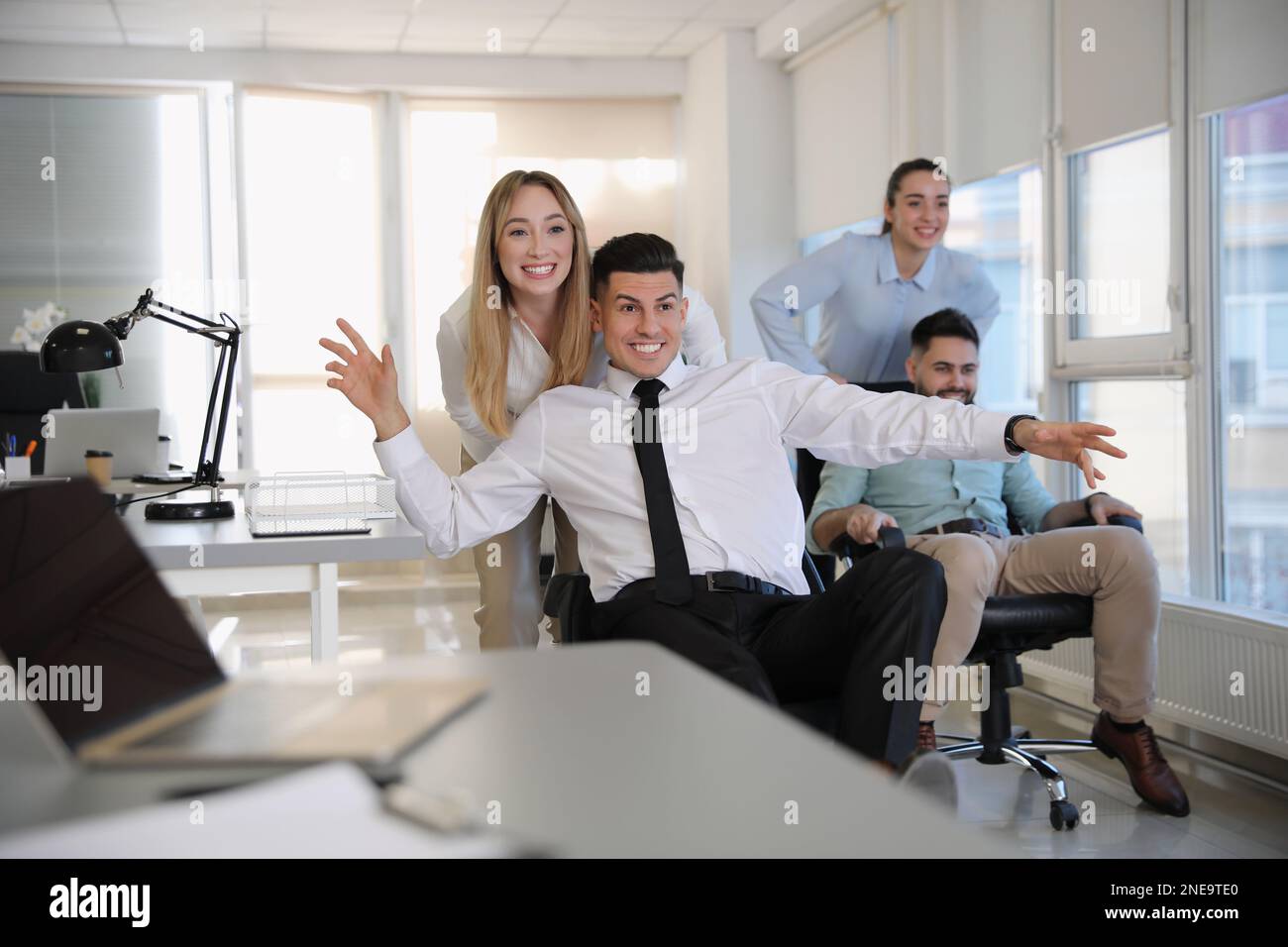 Happy office employees riding chairs at workplace Stock Photo - Alamy