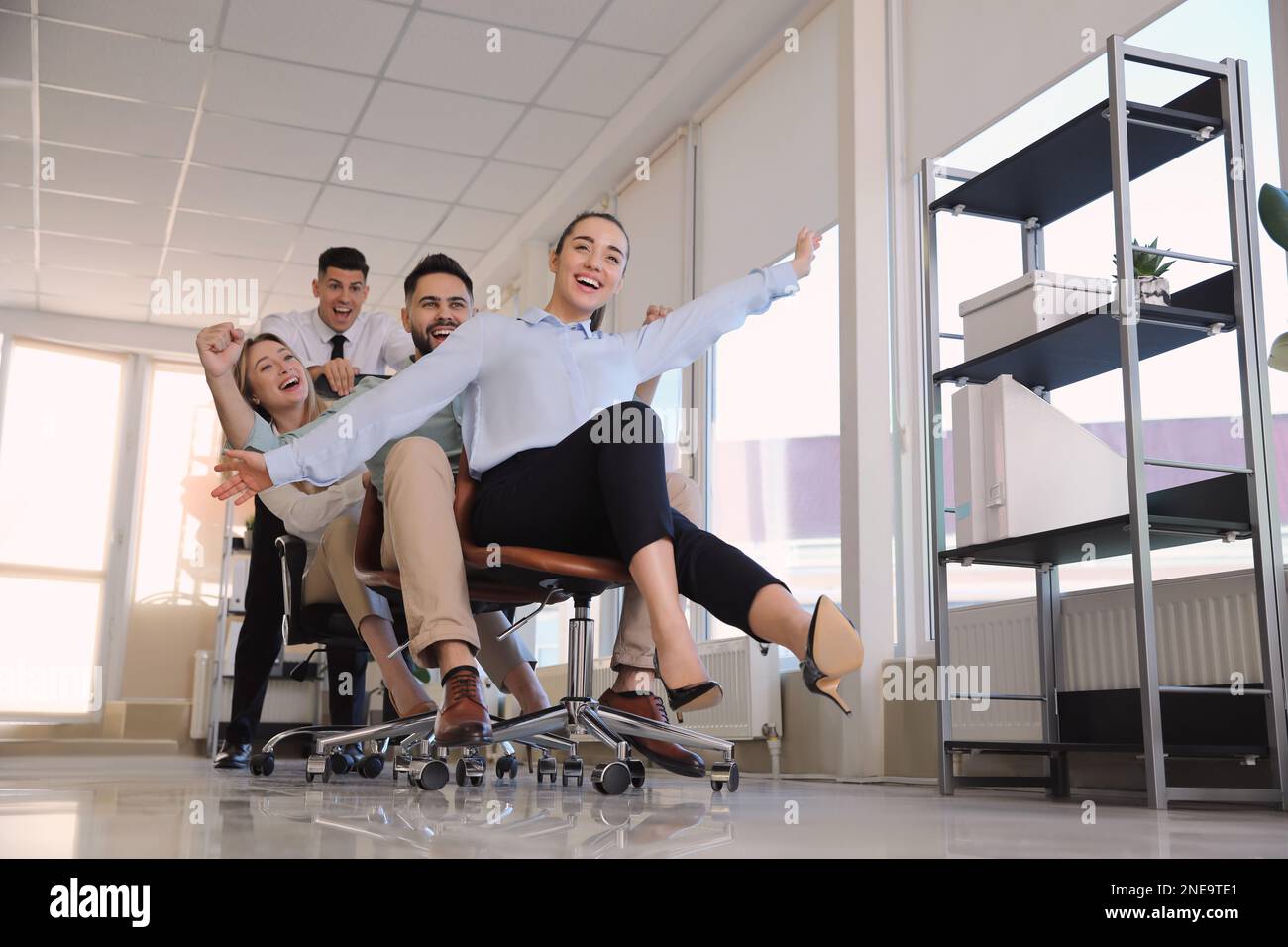 Happy office employees riding chairs at workplace Stock Photo - Alamy