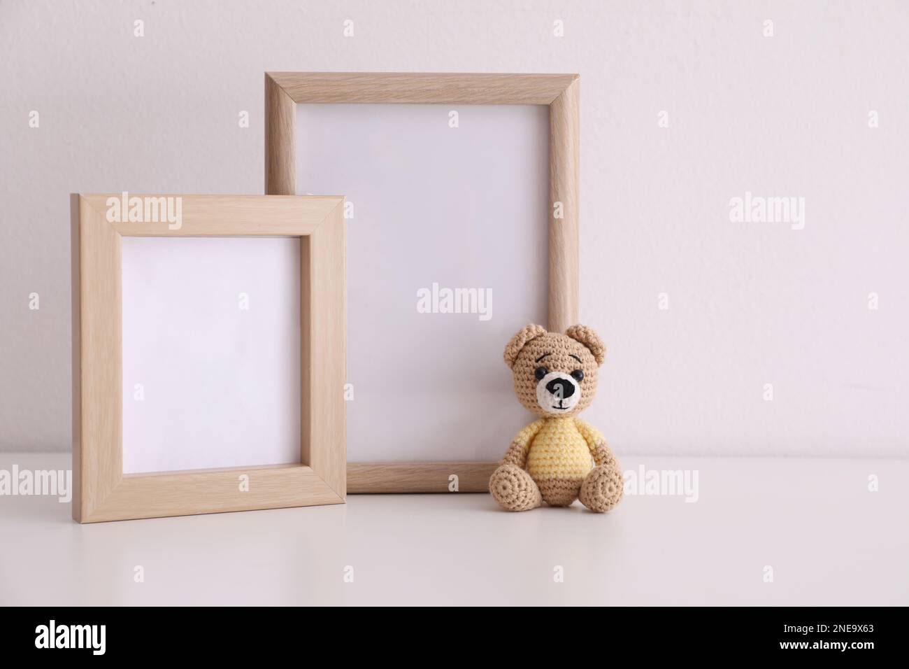 Empty photo frames and toy bear on table near white wall. Space for ...