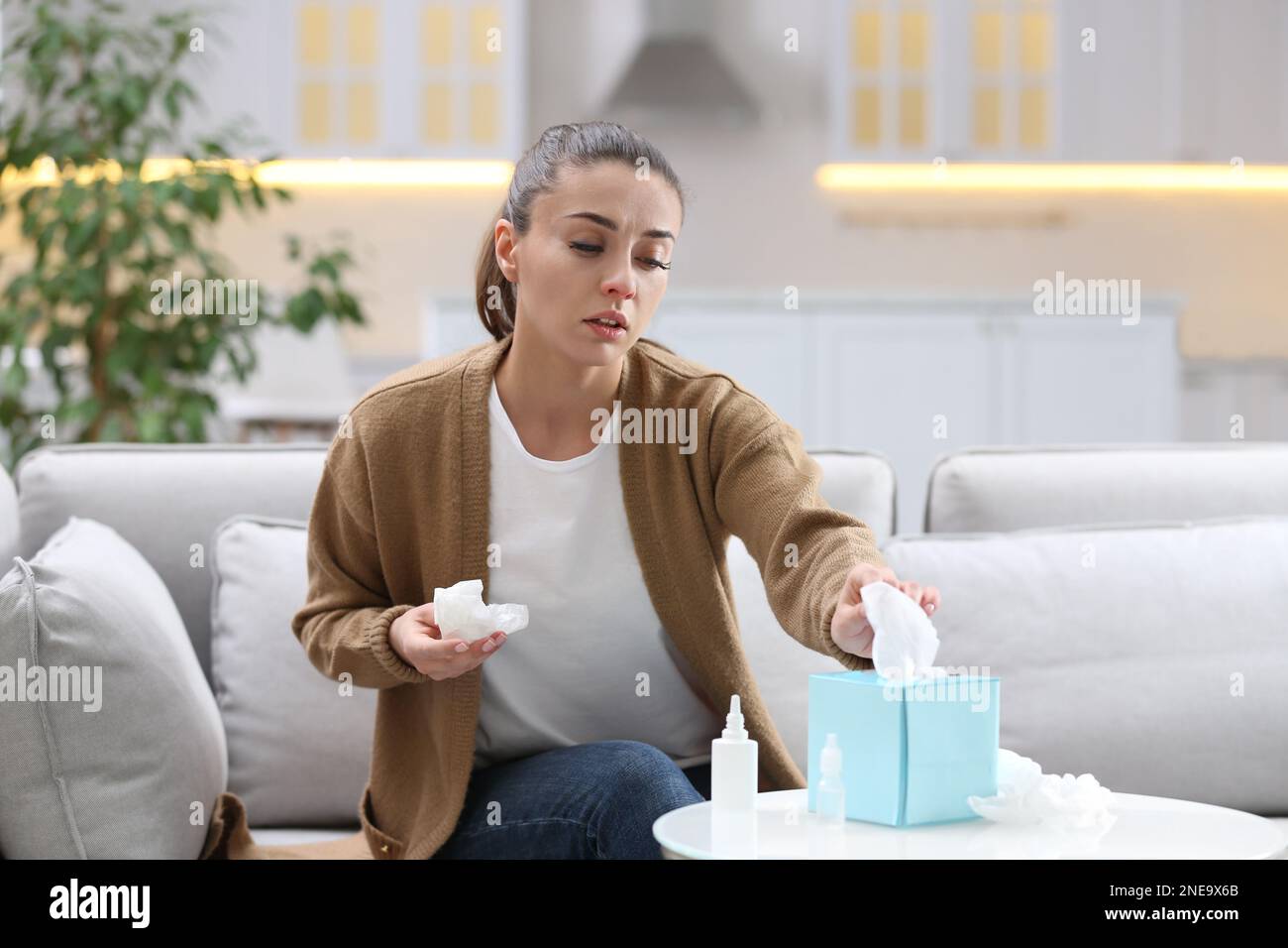 Sick woman with nasal spray, drops and box of paper tissues on sofa at ...