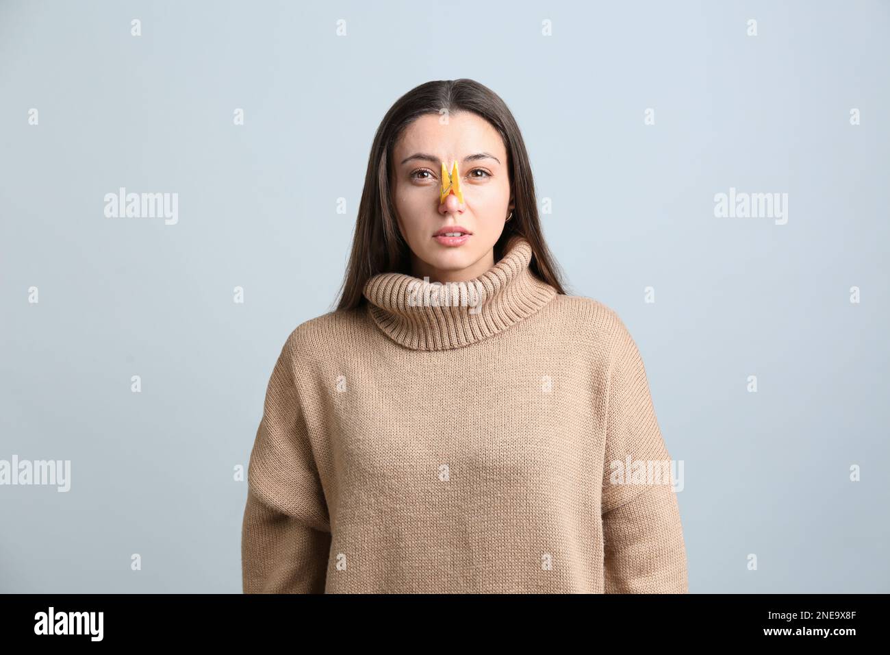 Young woman with clothespin on light grey background. Runny nose ...