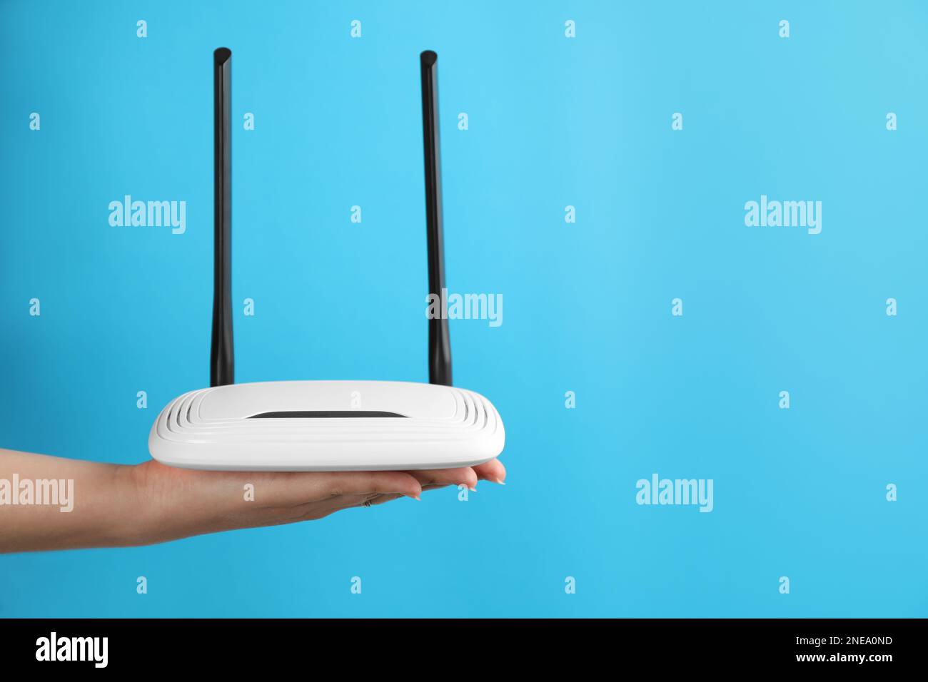 Woman holding modern Wi-Fi router on light blue background, closeup ...