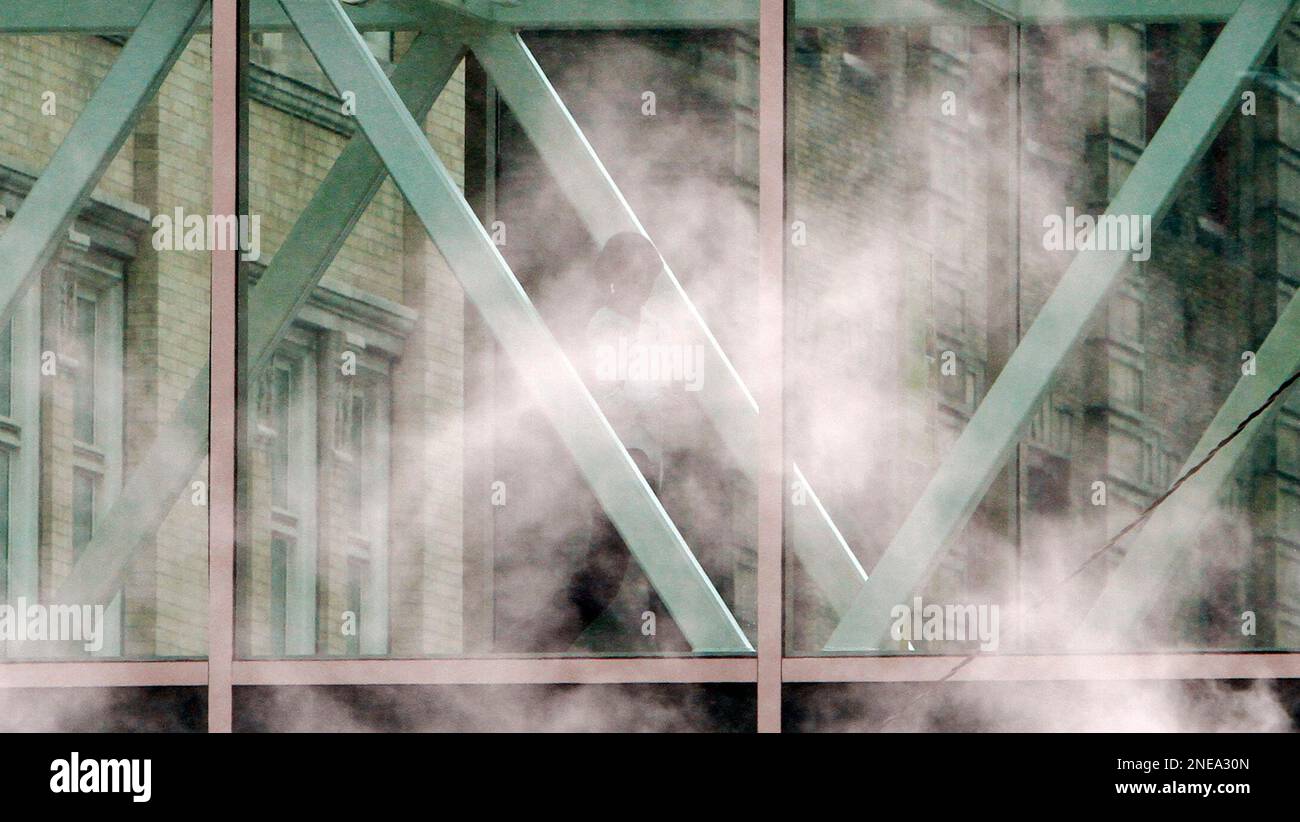 Steam from vents below envelops an enclosed overhead walkway as a woman ...