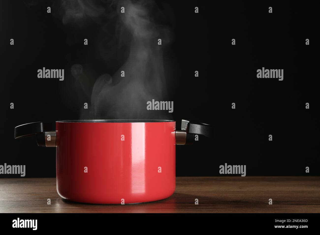 Pot with steam on wooden table against black background, space for text ...