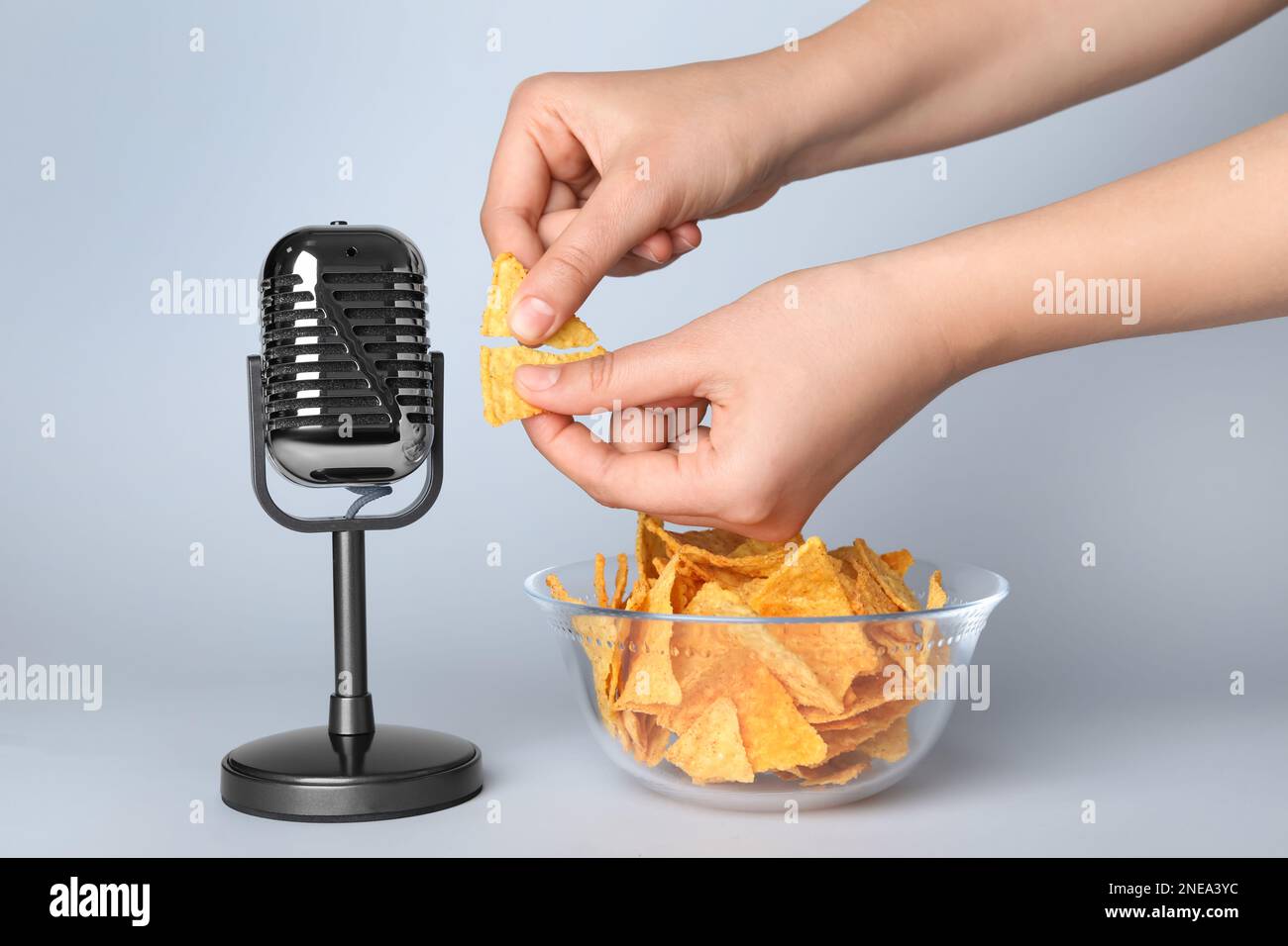 Woman making ASMR sounds with microphone and nacho chip on grey ...