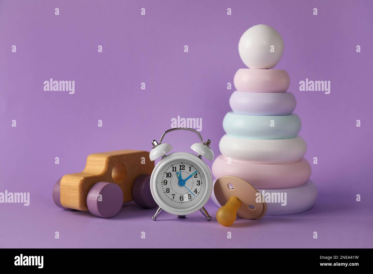 Alarm clock, toys and baby dummy on violet background. Time to give ...