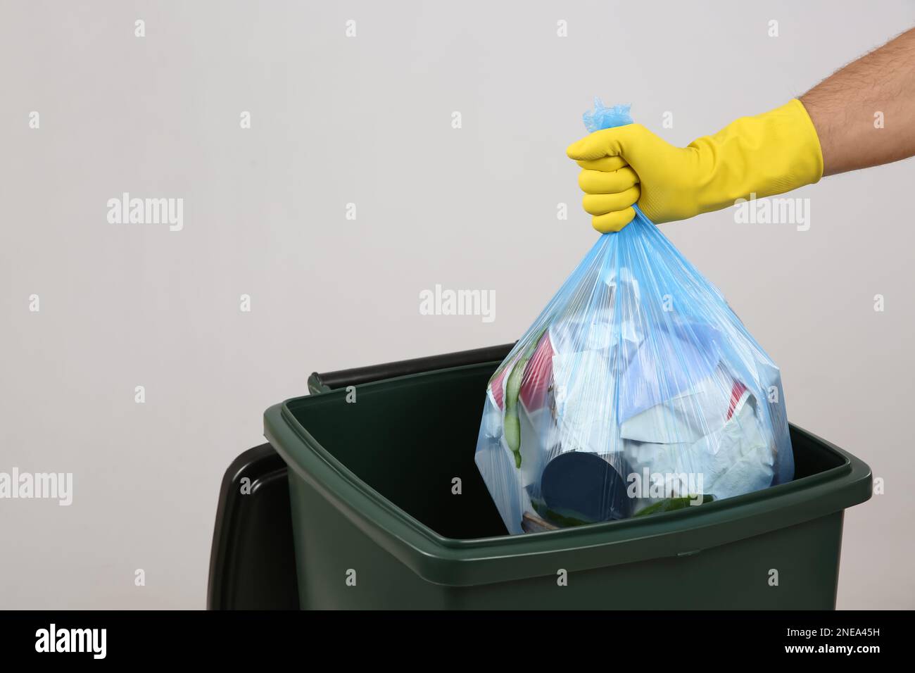 Man throwing garbage bag into bin on light background, closeup. Space ...