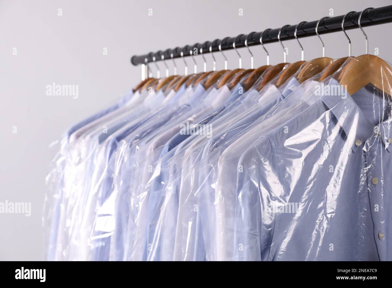 Hangers with shirts in dry cleaning plastic bags on rack against light ...