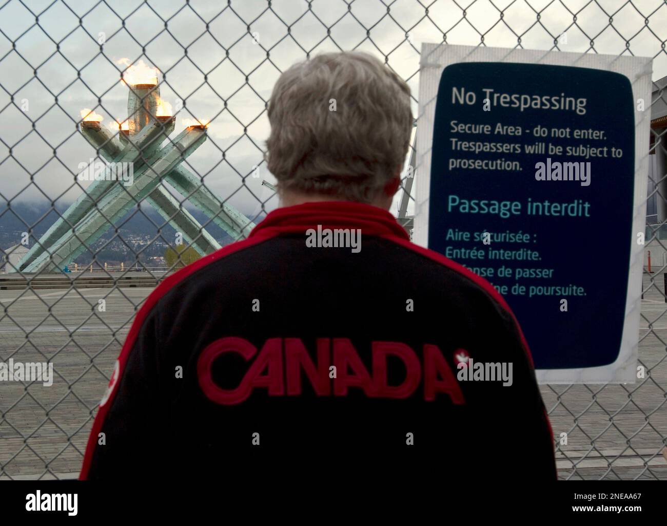 A visitor looks through a chain link fence at the Olympic cauldron at ...