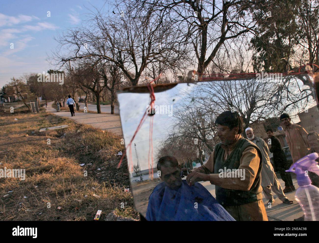 A Pakistani street barber is seen reflected in a mirror giving a ...