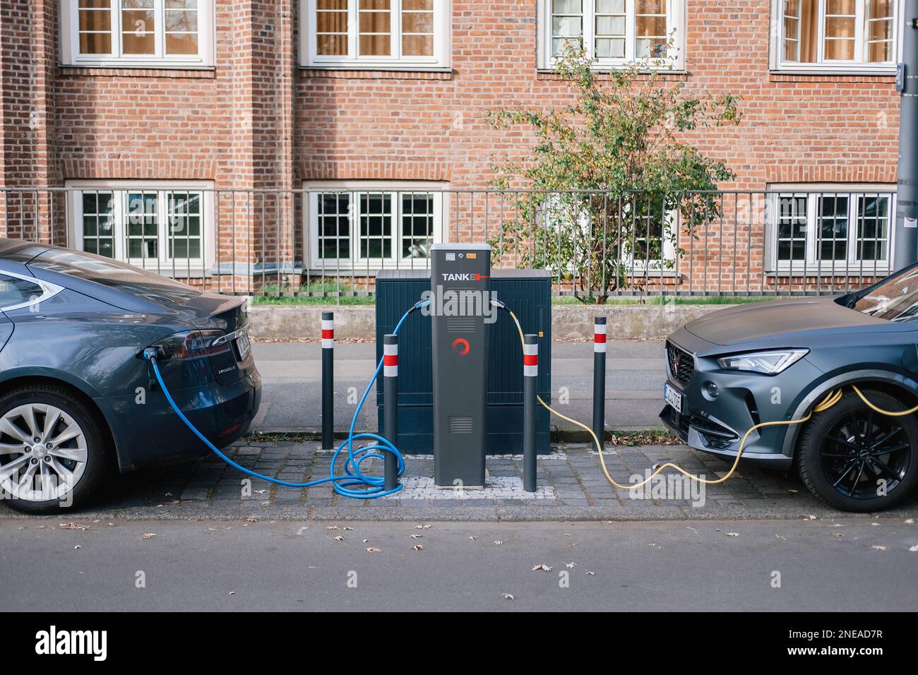 Two electric cars charge their batteries at a charging station. E-cars are the green future and ...