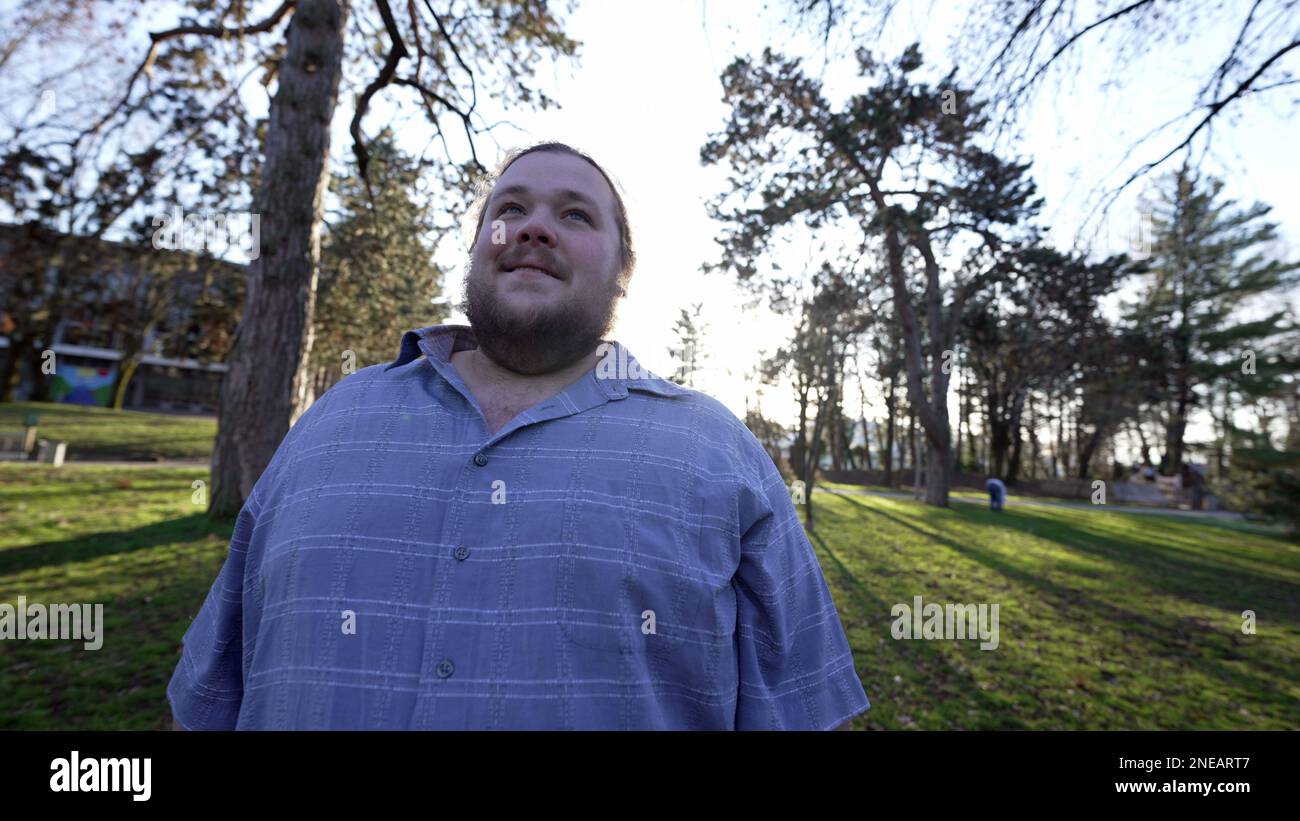 One contemplative chubby young man walking outdoors at park feeling ...