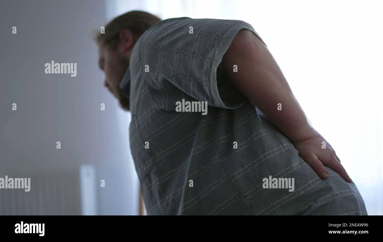 One overweight man having back pain by getting up from couch. A ...