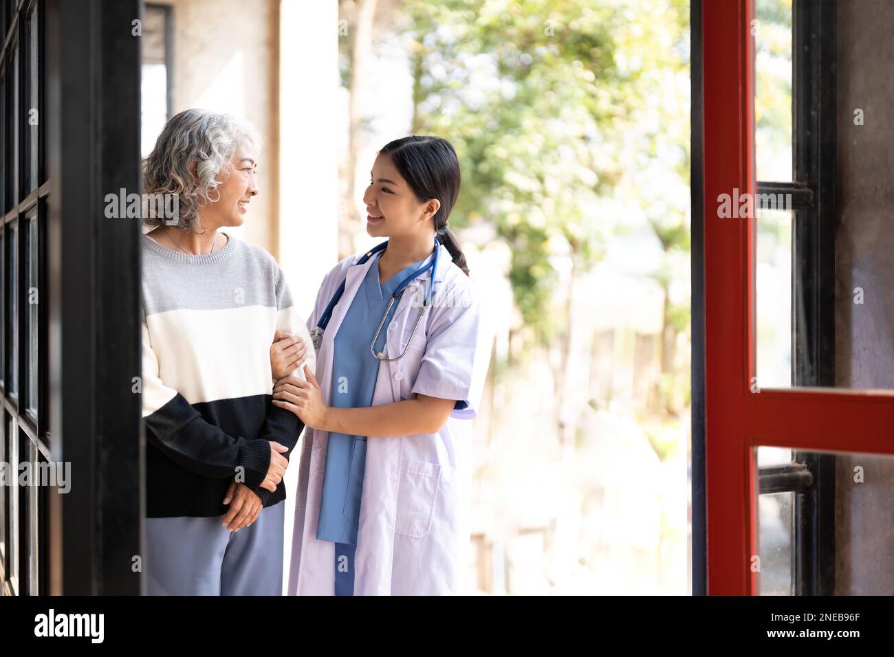 Young caregiver helping senior woman walking. Nurse assisting her old woman patient at nursing ...
