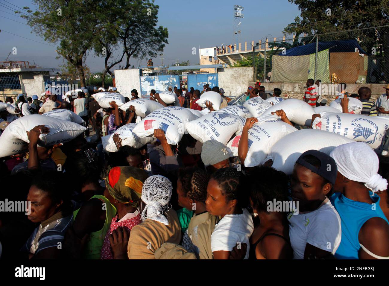 Women wait in line as others carry bags of rice on their heads at a ...