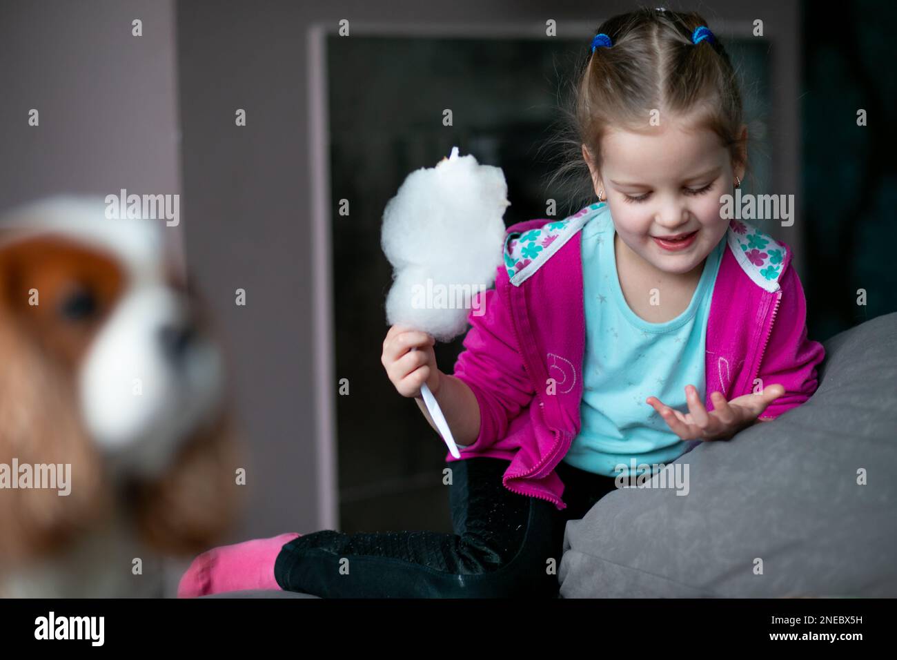 Portrait of smiling little girl holding candyfloss, looking at sticky ...