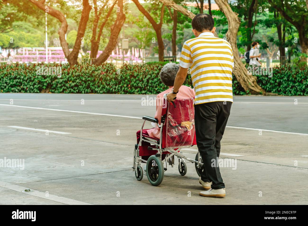 Back view of Asian elderly man walking with disabled elderly woman ...