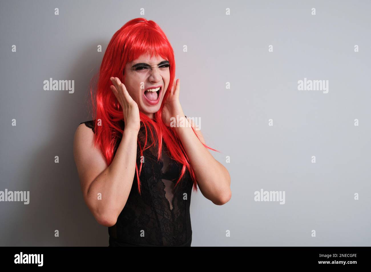 Portrait of drag queen screaming and wearing a red wig on grey ...