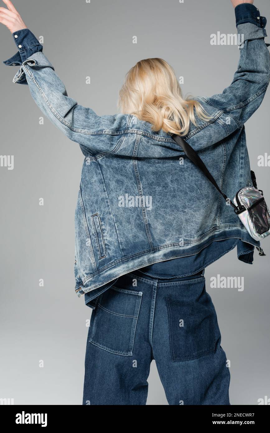 back view of young blonde model in stylish denim jacket with belt bag ...