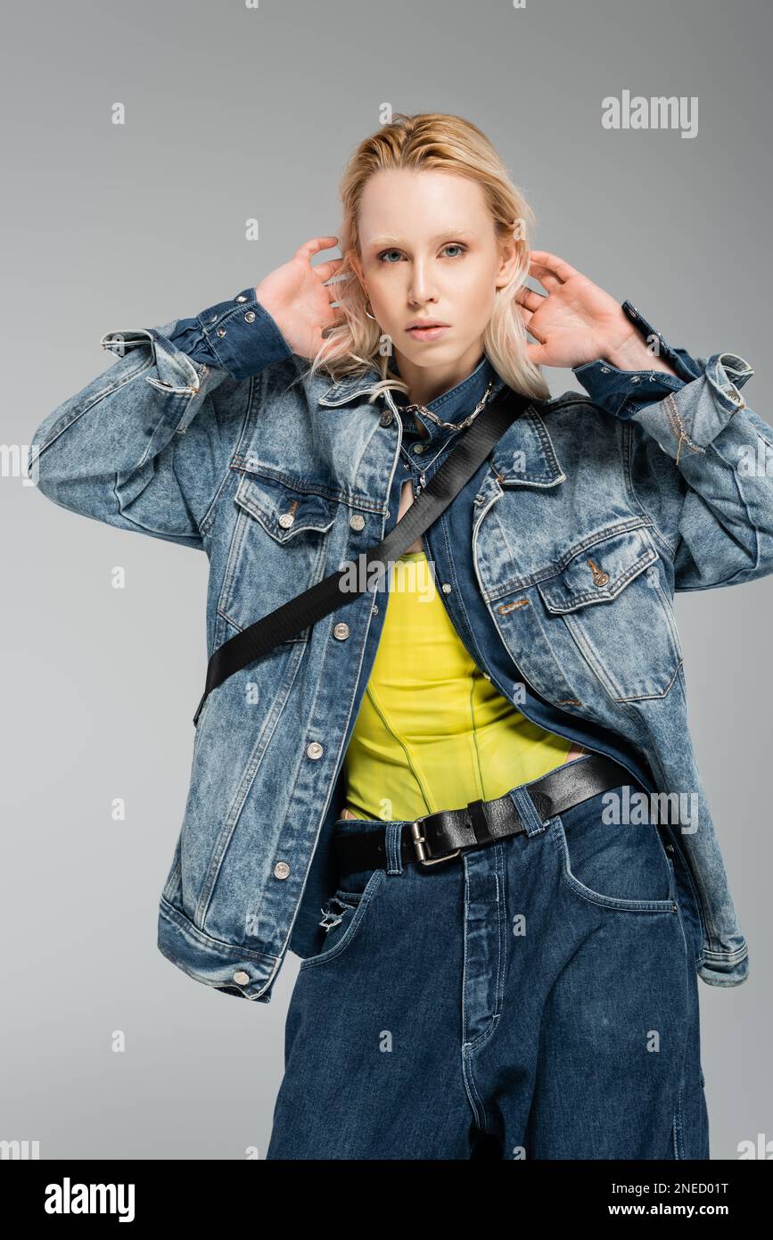 young blonde woman in stylish denim outfit looking at camera while ...
