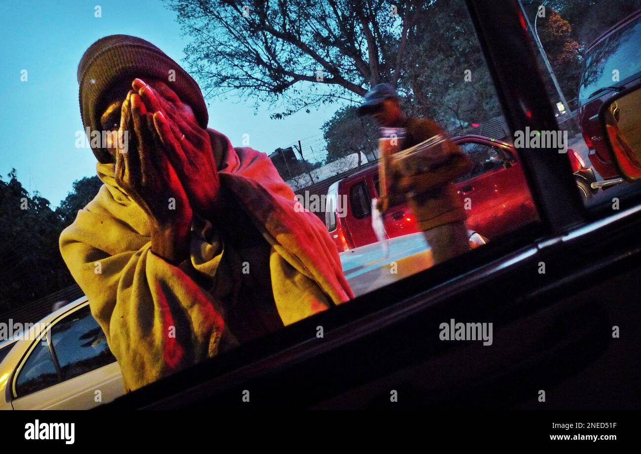 A homeless Indian man begs at the window of a car in traffic on a ...
