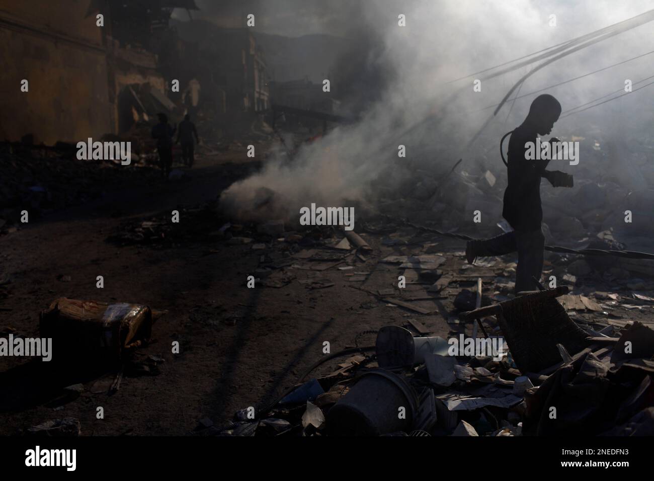 A young man walks by a smoldering fire of burning trash among ...