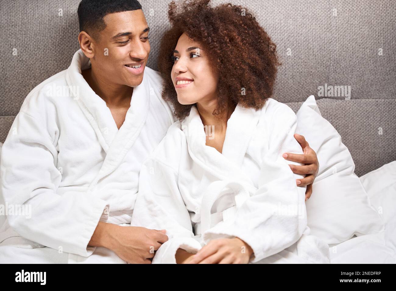 Young man and woman sit hugging each other on bed Stock Photo - Alamy