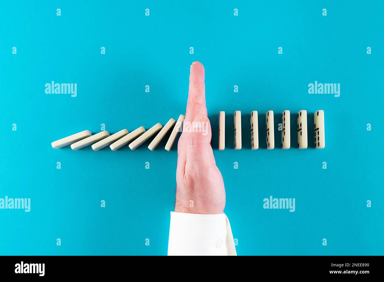 top view of male hand preventing line of domino tiles from toppling and ...