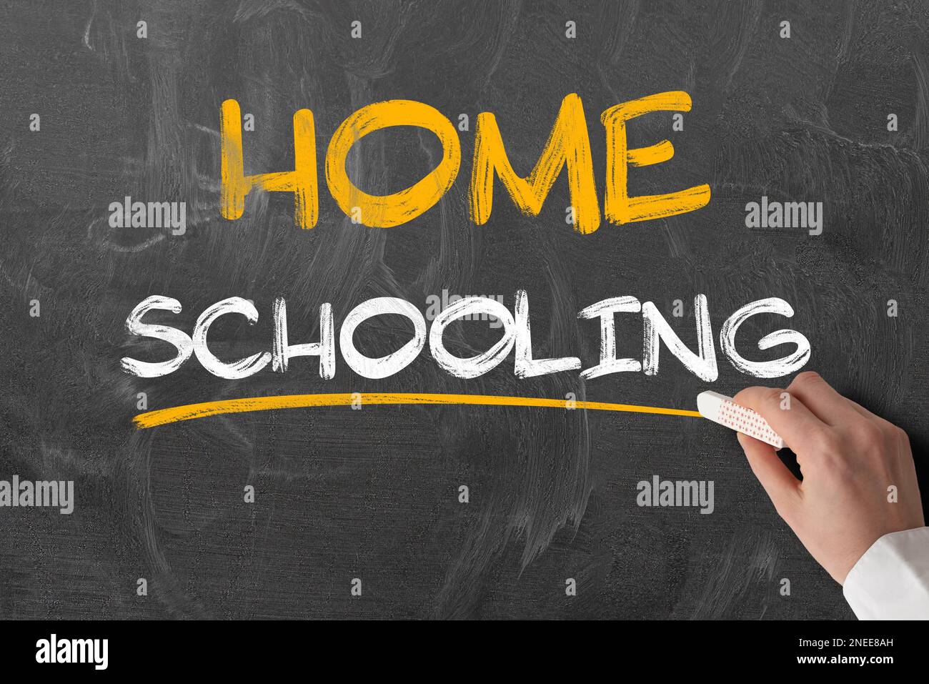 hand holding piece of chalk against blackboard with text HOME SCHOOLING ...