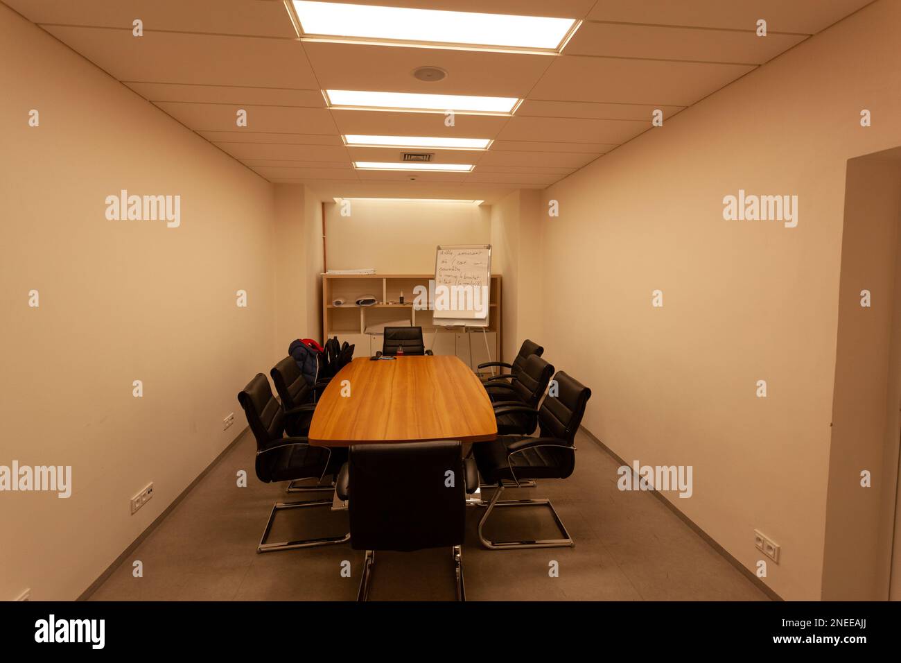 Black chairs are around a conference table lit by square lights in the ...