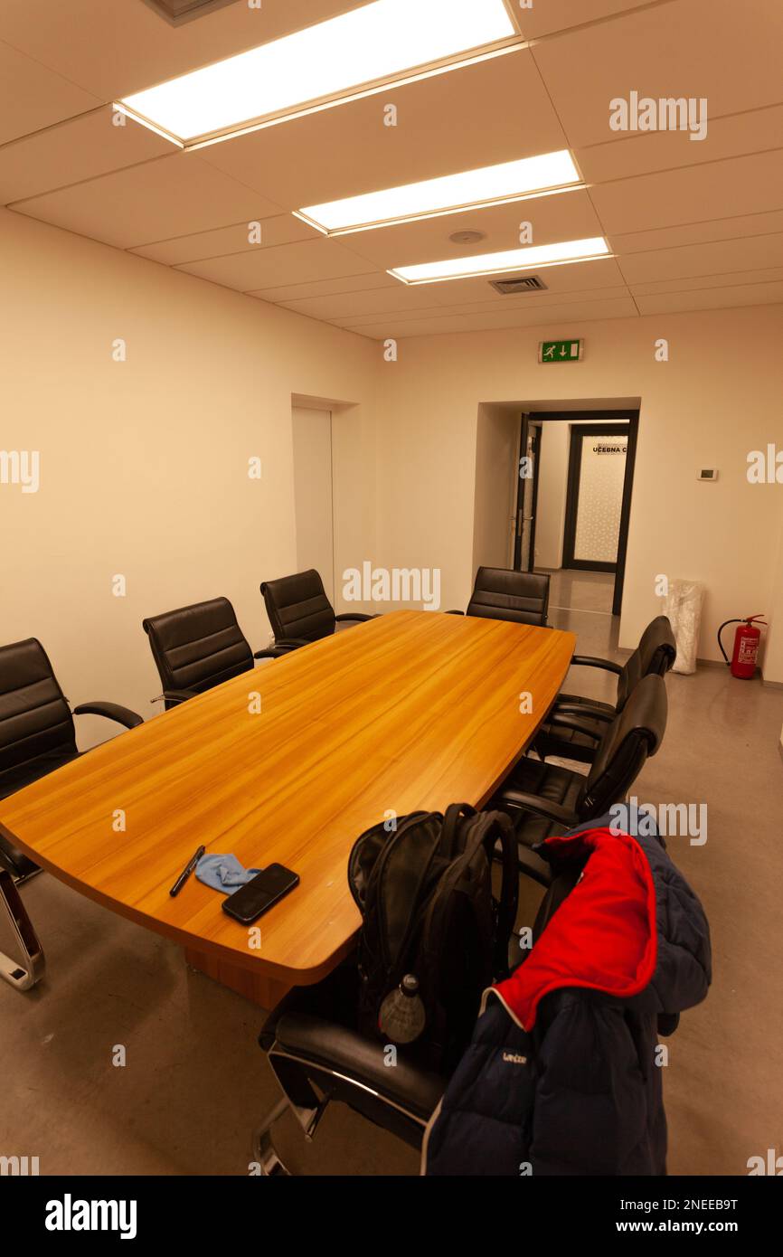 Black chairs are around a conference table lit by square lights in the ...