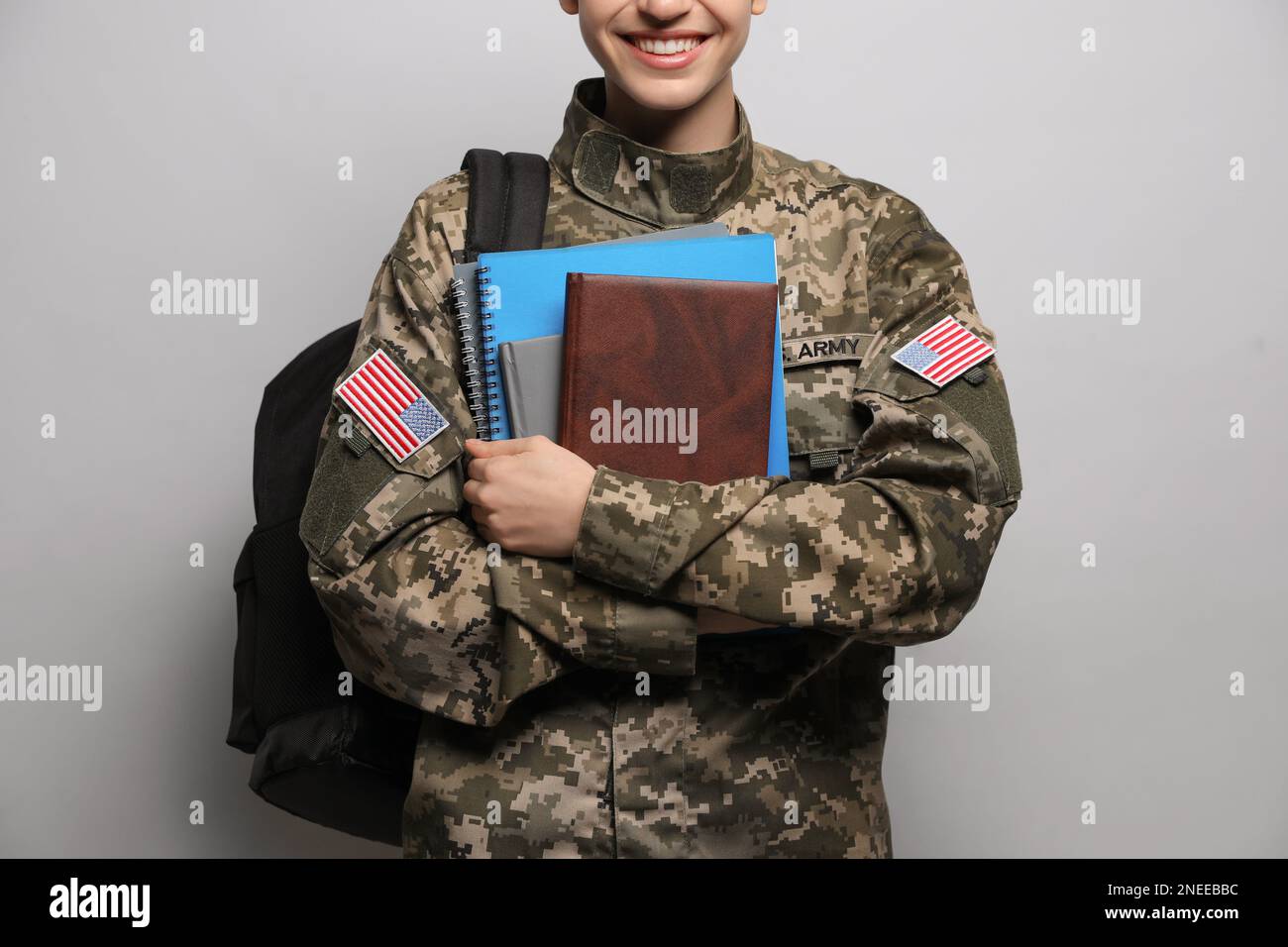 Female cadet with backpack and notebooks on light grey background ...