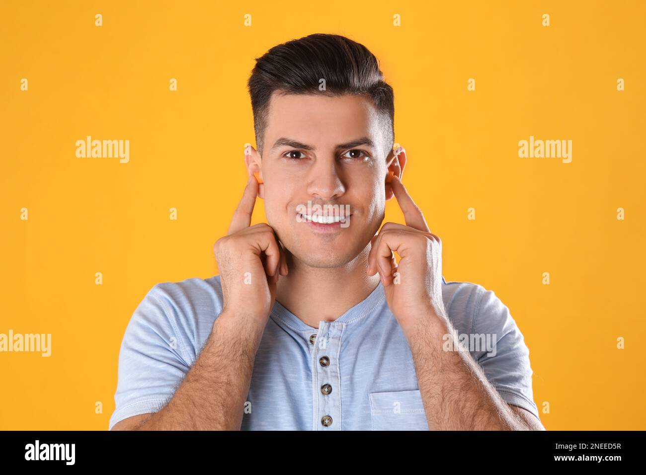 Man inserting foam ear plugs on yellow background Stock Photo - Alamy