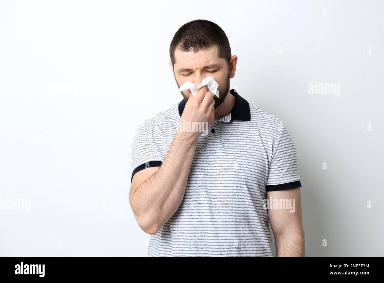 Man with tissue suffering from runny nose on white background Stock ...