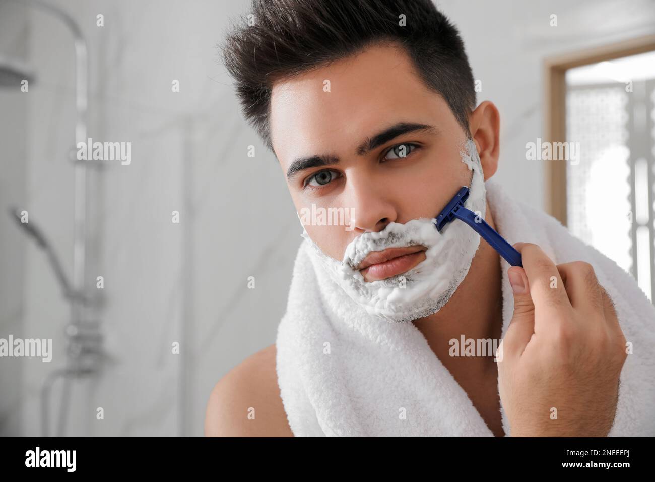 Handsome young man shaving with razor in bathroom, space for text Stock ...