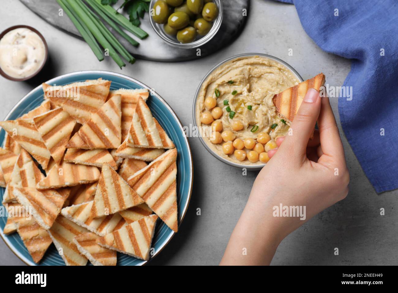 Woman dipping pita chip into hummus at grey table, top view Stock Photo ...